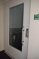 Porta de saída de incêndio com painel de vidro, alarme de incêndio e sinal de acessibilidade para cadeiras de rodas.
