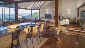 Uma sala de jantar moderna com uma mesa de vidro, cadeiras de vime e vista para o exterior.