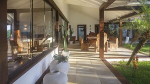 Um espaço ao ar livre coberto, com um pátio, móveis de madeira e plantas em vasos.