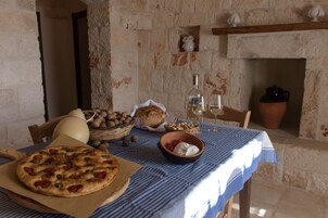 Uma mesa rústica com pizza, bowls de nozes e queijo, e taças de vinho.
