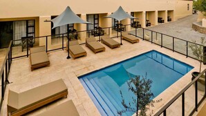 Área de piscina no terraço, com espreguiçadeiras e guarda-sóis, cercada por um grade baixo.