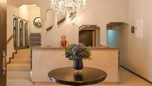 Um saguão de hotel com uma mesa redonda, um candelabro, um balcão de recepção e uma escadaria.
