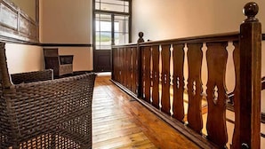 Uma escadaria de madeira com guarda-corpo que leva a um quarto com uma cadeira de vime e uma janela.
