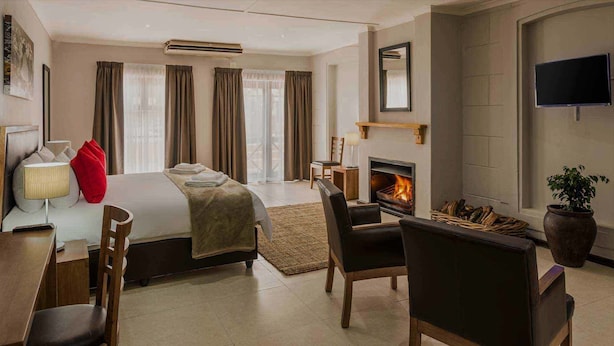 Quarto de hotel com cama, escrivaninha, poltrona, lareira e televisão.
