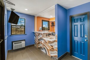 Uma área de recepção com balcão de padrão marmorizado, uma porta azul e uma janela com vista para um estacionamento.