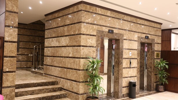 Um hall de entrada com piso de mármore e escadaria que leva a elevadores indicados com os números 3 e 6.