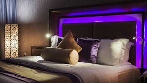 Quarto de hotel com cama, almofadas, mesa de cabeceira e luminária fixada na parede.