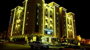 Hotel com vários andares, fachada iluminada, entrada destacada e estacionamento com diversos veículos.