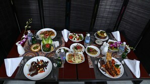Mesa posta com diversos pratos, incluindo saladas, carnes e legumes, acompanhados de condimentos e garrafas de água.