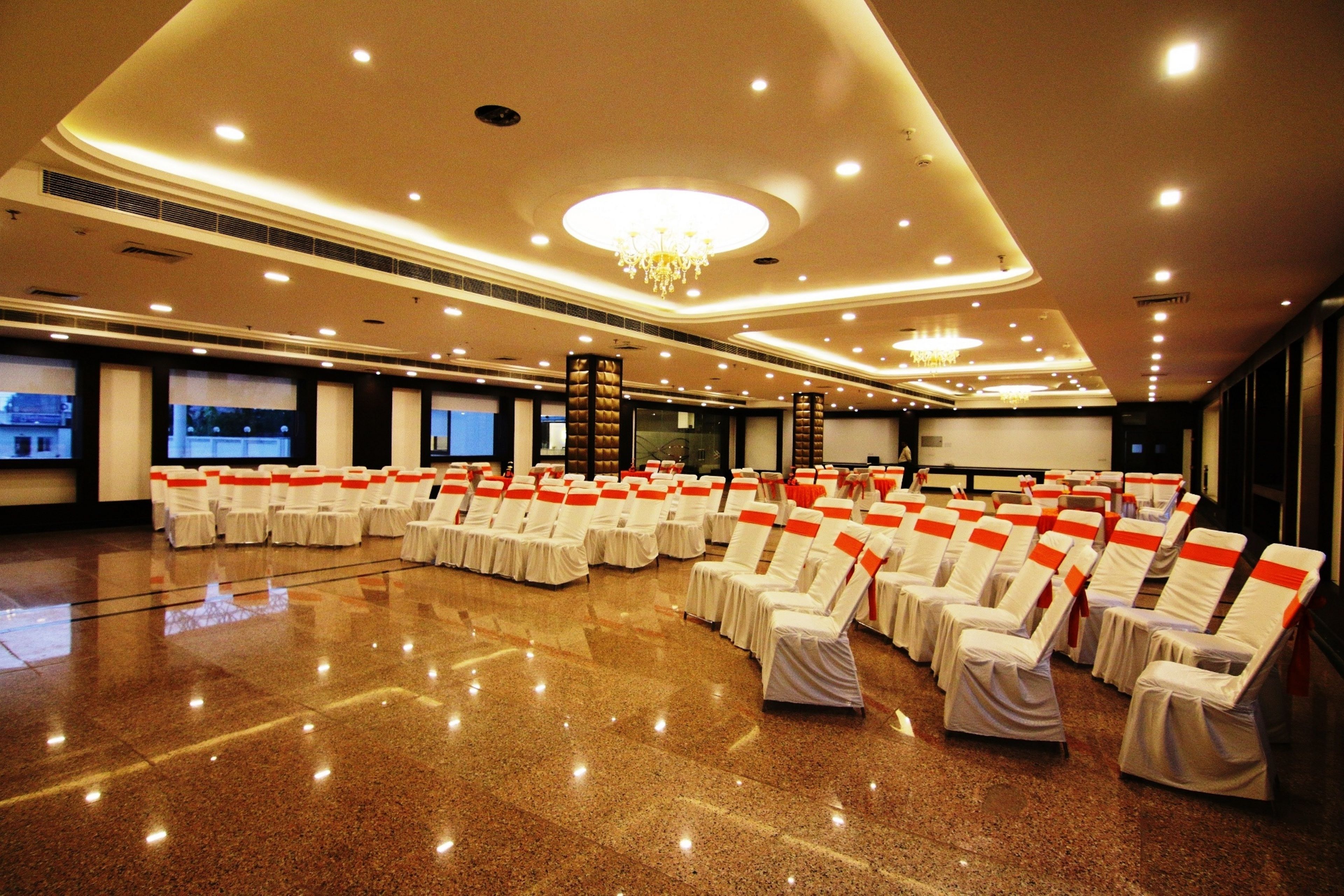 Uma sala de conferências com fileiras de cadeiras, uma tela grande e um lustre.