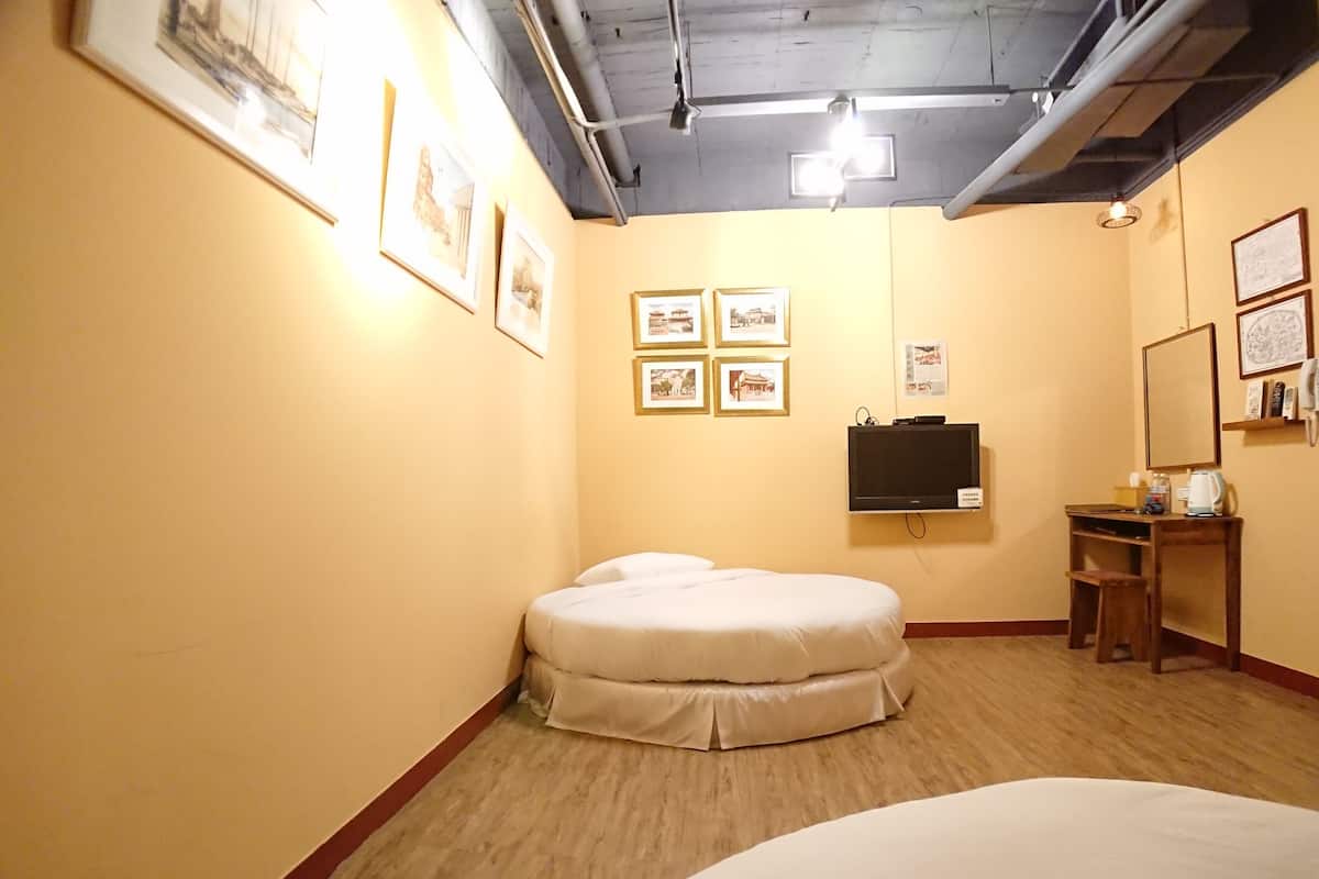 Quarto de hotel com cama, escrivaninha com cadeira, televisão de tela plana e quadros nas paredes.