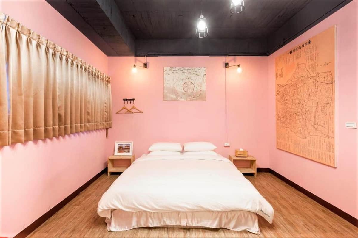 Quarto com cama grande, piso de madeira, paredes cor de rosa e um mapa na parede.