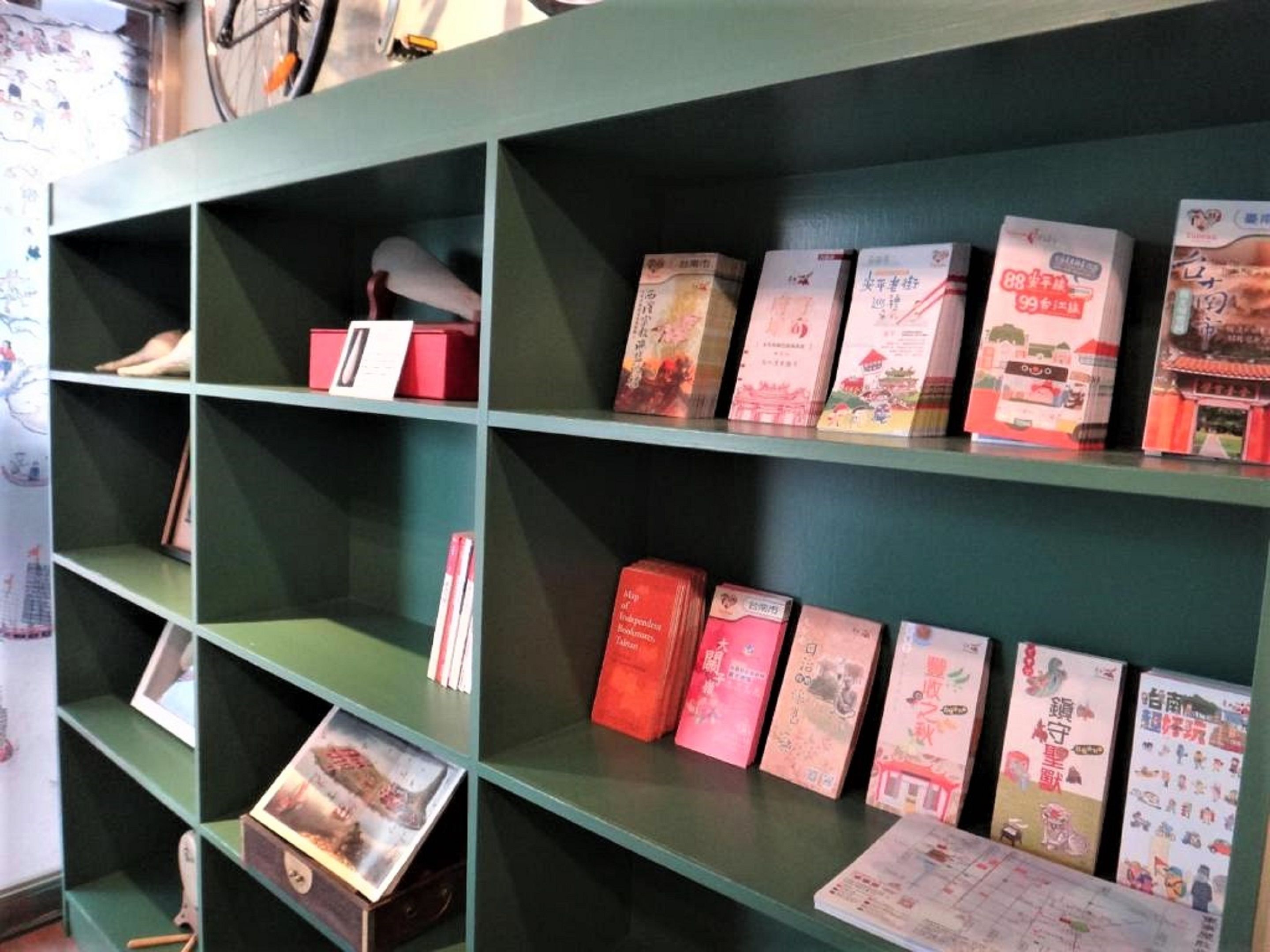 Uma estante verde com vários livros e um quadro emoldurado.