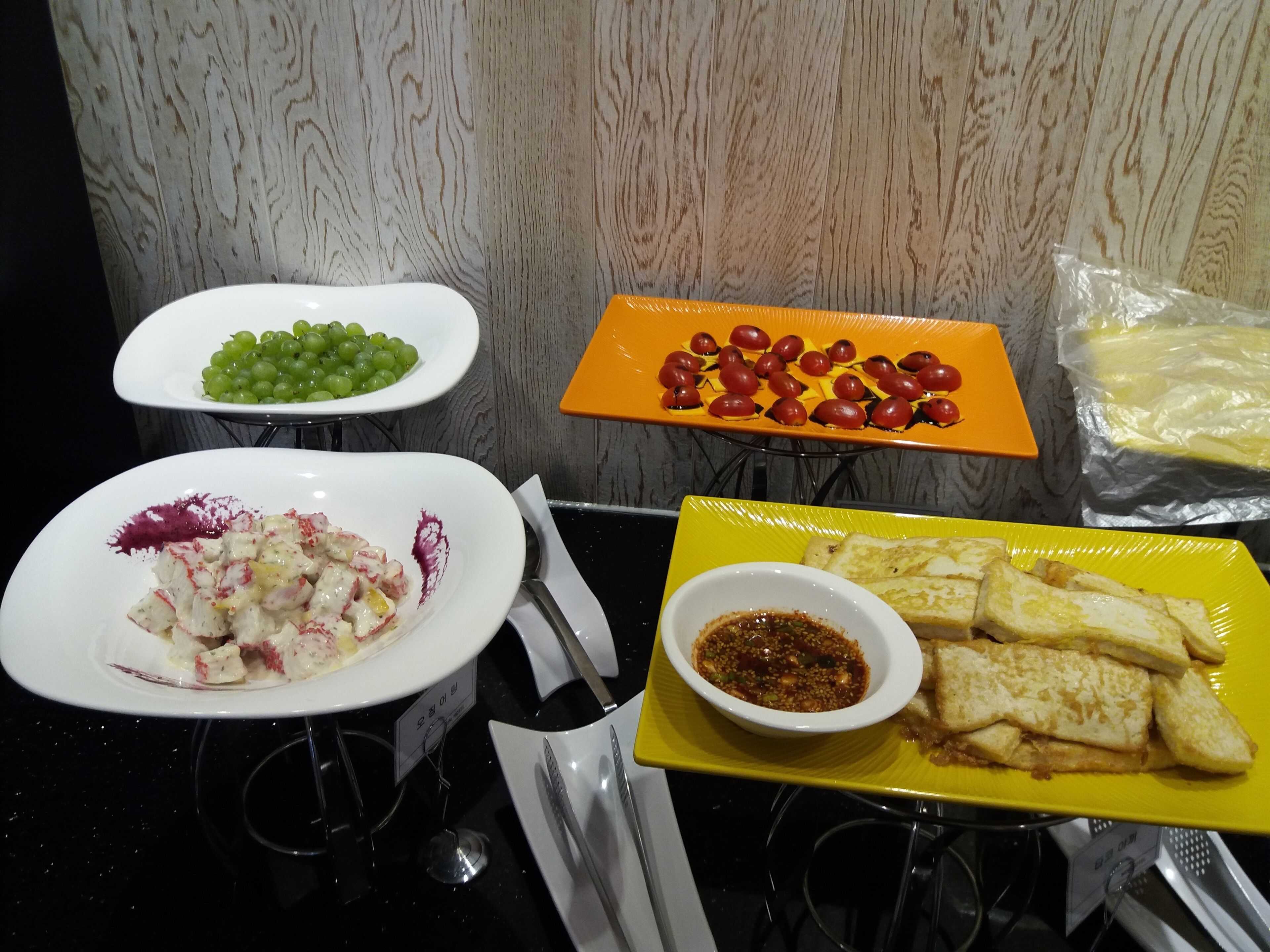 Uma mesa com diversos pratos, incluindo salada de frutos do mar, uvas verdes, tomates cereja e pão.