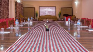 Uma sala de conferências com uma mesa comprida, cadeiras, garrafas de água e um tapete decorativo.