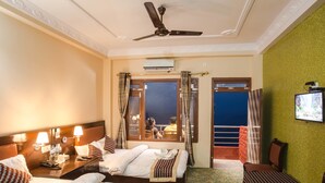 Quarto de hotel com duas camas, ventoinha no teto, aparelho de ar condicionado, televisão e varanda com vista.