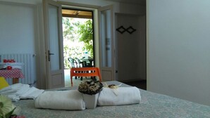 Quarto com uma cama, duas almofadas, uma mesa pequena com toalha quadriculada e uma cadeira.