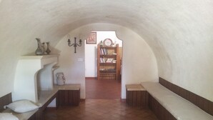 Um corredor estreito e arqueado, com bancos em ambos os lados, piso de azulejos e uma estante de livros ao fundo.
