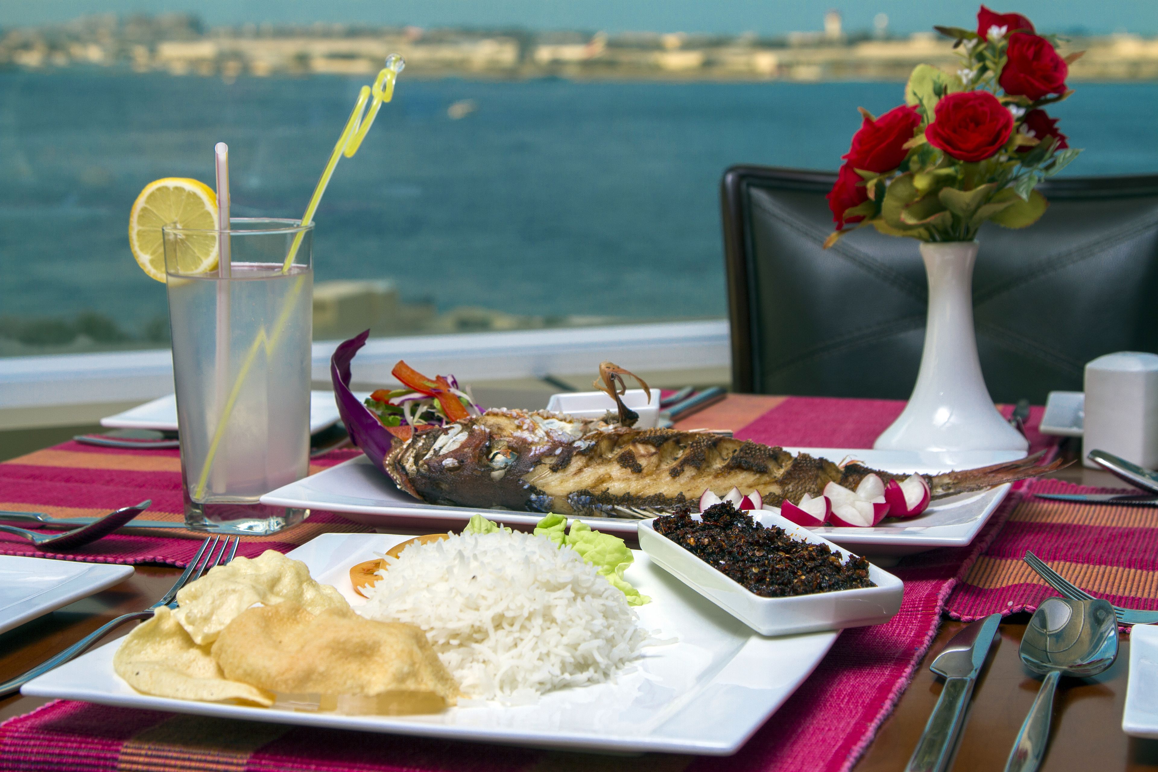 Uma mesa com uma refeição de arroz, peixe e salada, com vista para o litoral.