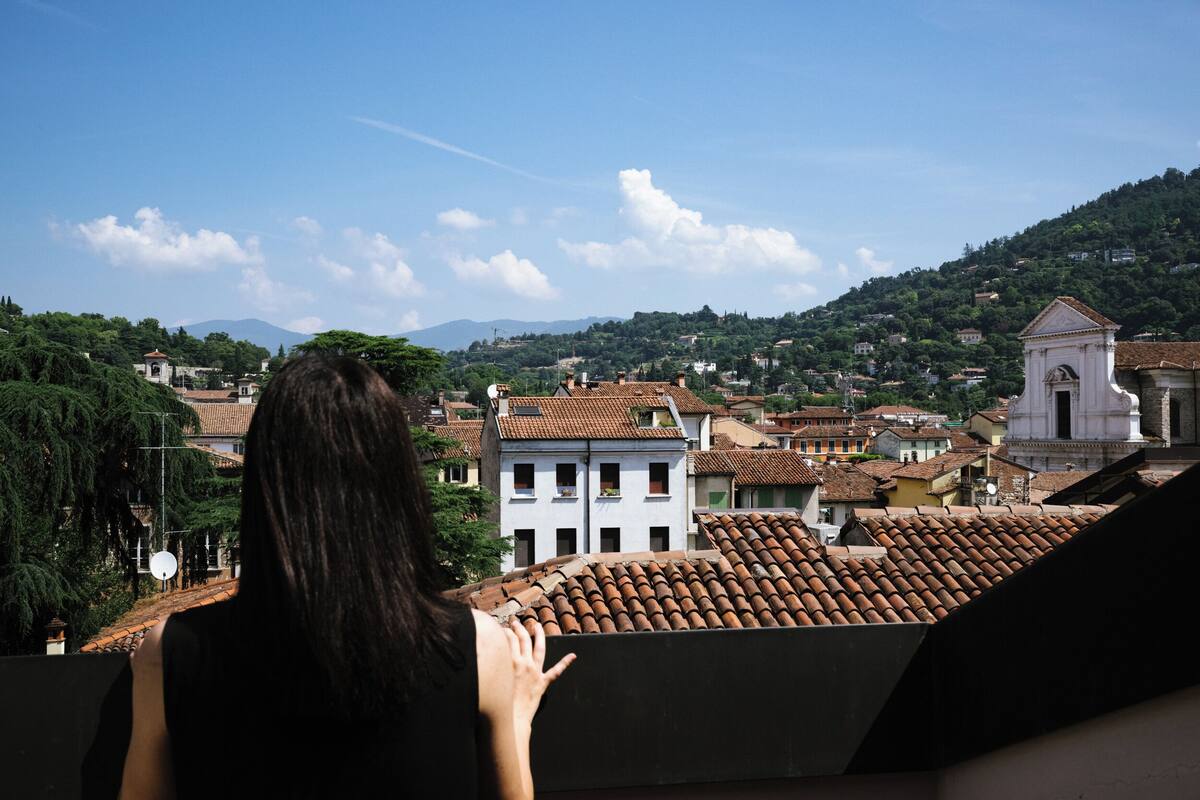 Mulher observa uma cidade com telhados de terracota e uma igreja.