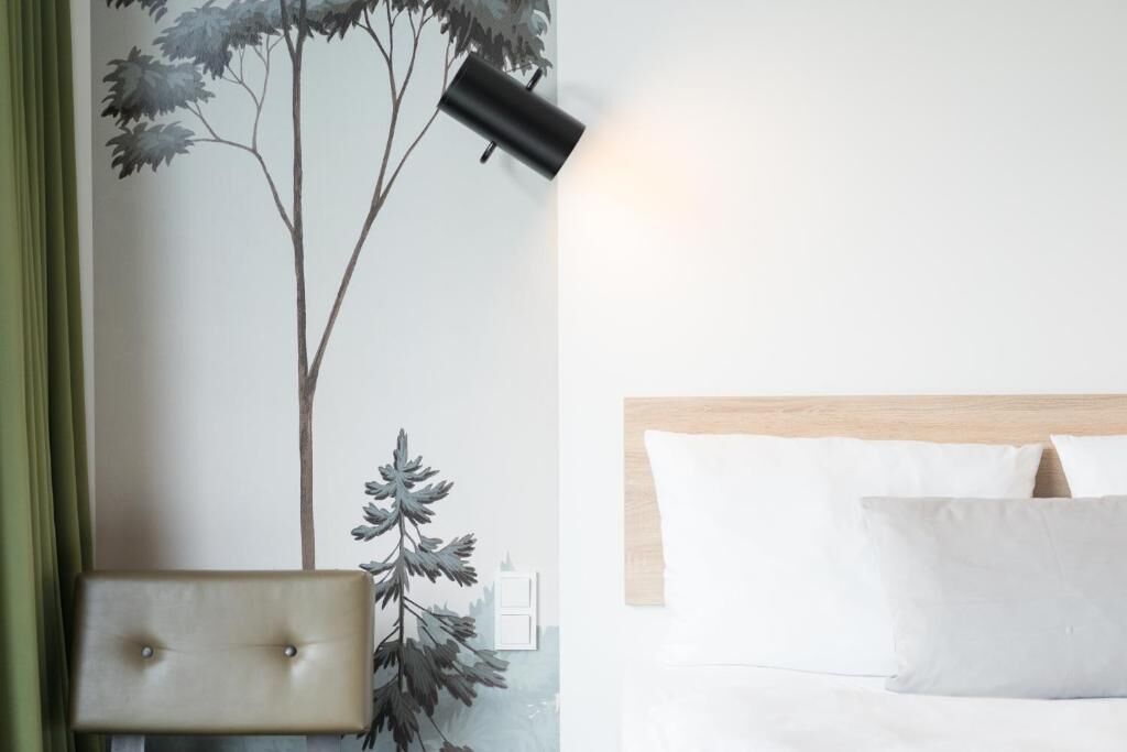 Quarto com cama, mesa de cabeceira, luminária na parede e planta suspensa.