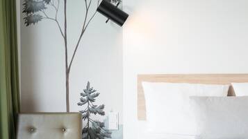 Quarto com cama, mesa de cabeceira, luminária na parede e planta suspensa.