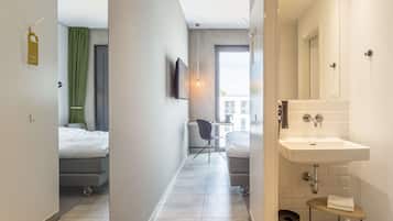 Quarto de hotel moderno com cama, escrivaninha, cadeira, banheiro com pia e vista para a cidade.