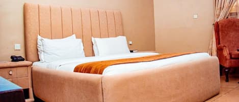 Quarto de hotel padrão com uma cama, uma mesa de cabeceira, uma cadeira e uma parede com duas molduras.