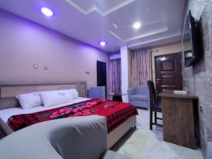 Quarto de hotel com cama, escrivaninha, cadeira, televisão e ar condicionado.