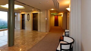 Um hall de hotel com piso de mármore, balcão de recepção e vista para a paisagem urbana através de grandes janelas.
