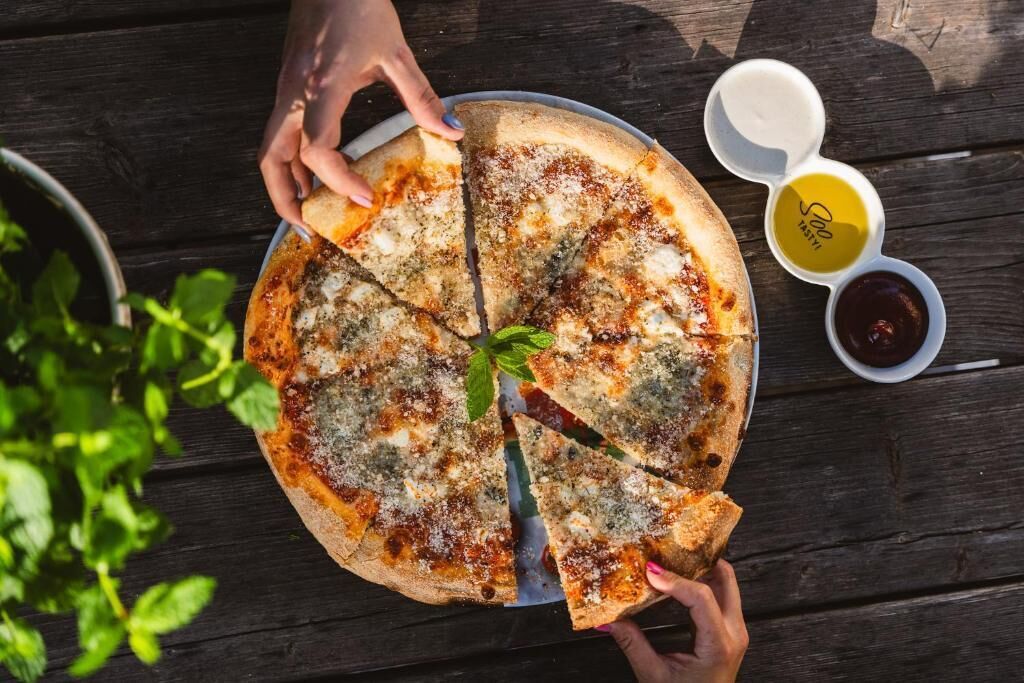 Pizza com fatias sendo servida, acompanhada por dois pequenos recipientes de acompanhamentos.