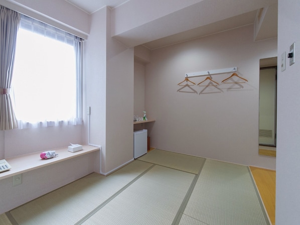 Quarto com piso de tatame, janela com cortinas, prateleira com objetos pessoais e um varal fixado na parede.