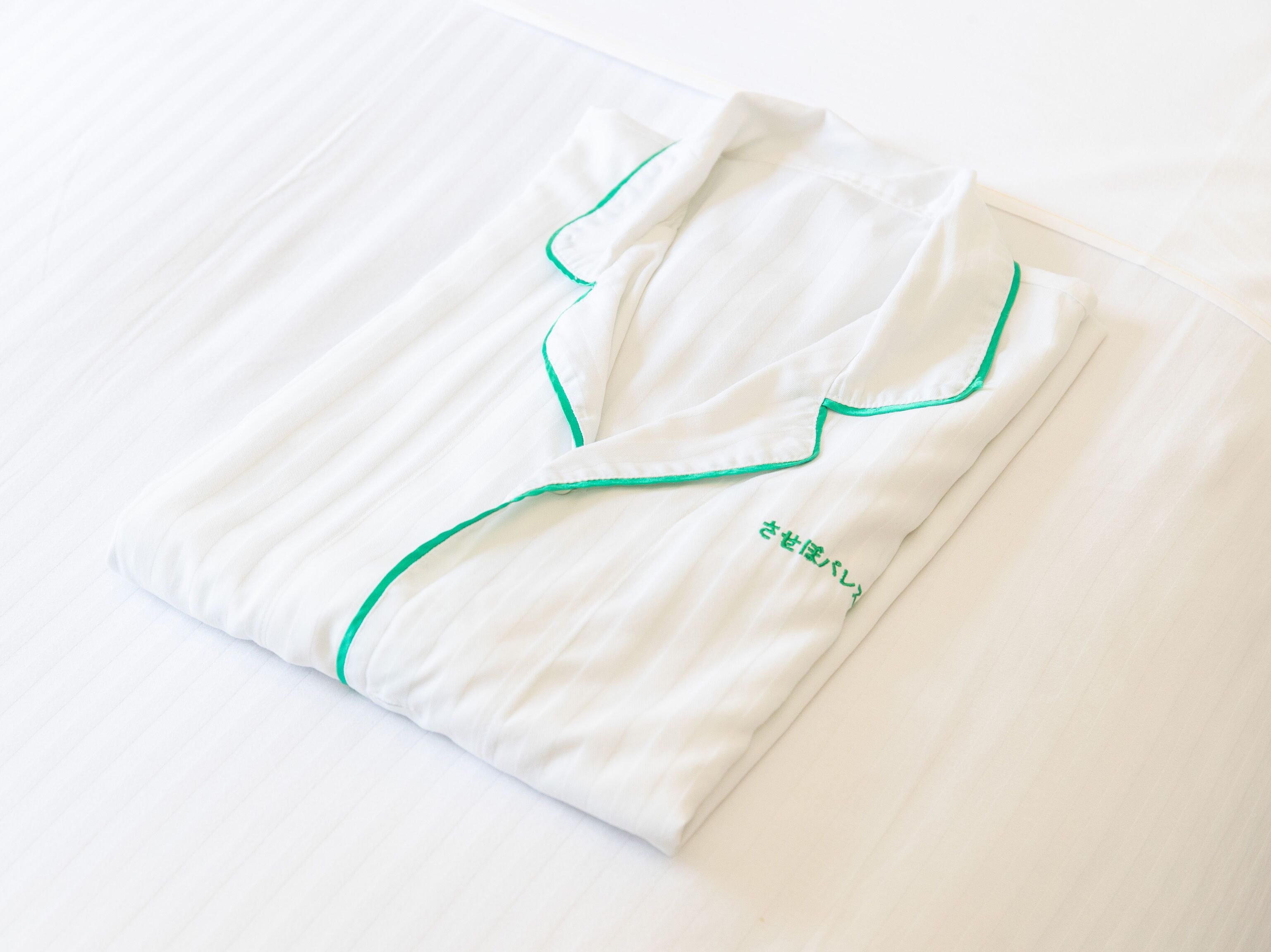 Uma camisa branca bem dobrada, com detalhes verdes e texto em japonês sobre uma superfície branca.