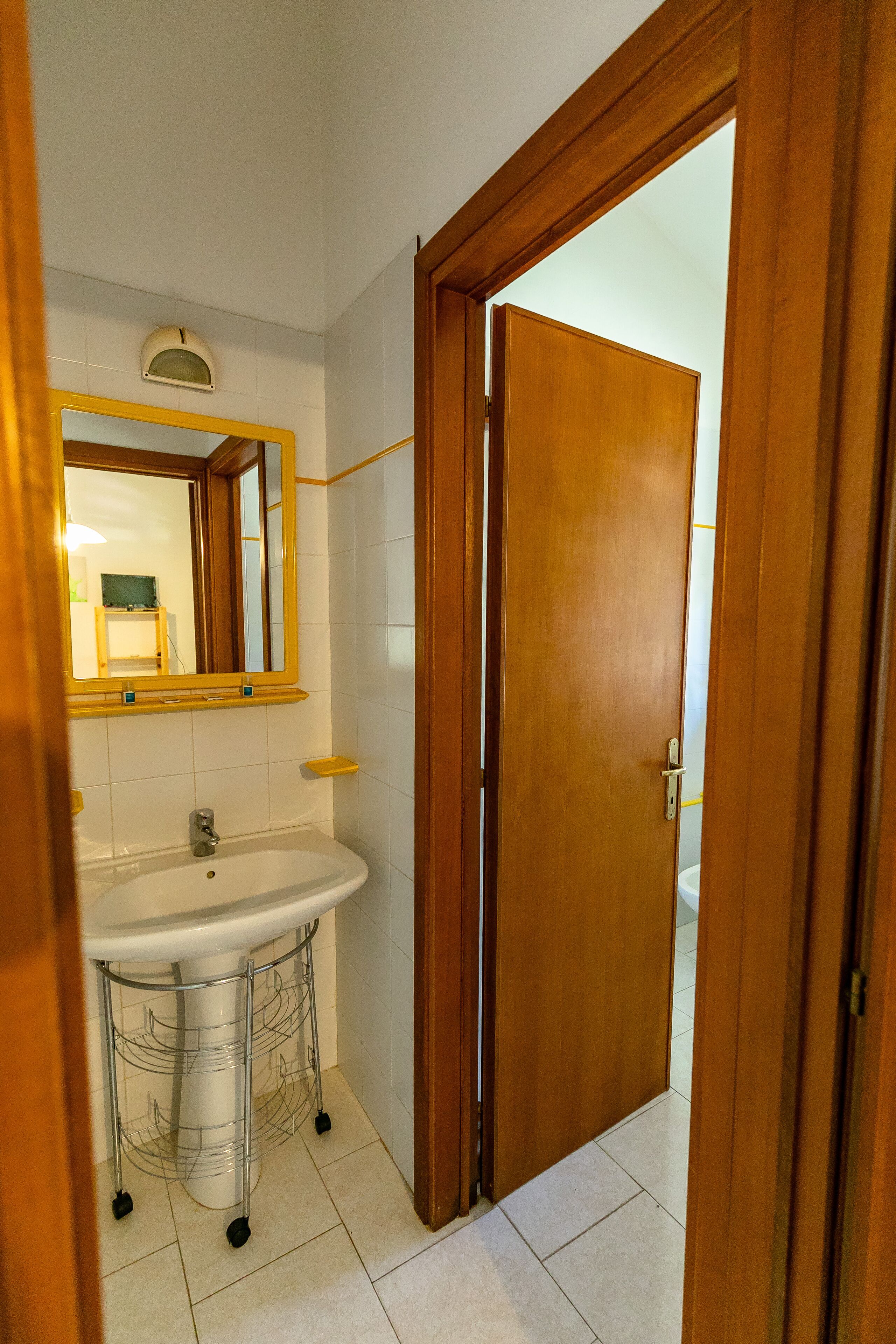 Casa de banho com lavatório branco, espelho com moldura de madeira e porta de madeira.