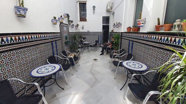Um pátio com piso de azulejos, cadeiras de metal preto e mesas com padrões azuis e brancos.