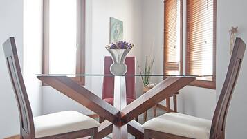 Uma área de refeições com mesa de vidro, cadeiras de madeira e luminária pendente roxa.