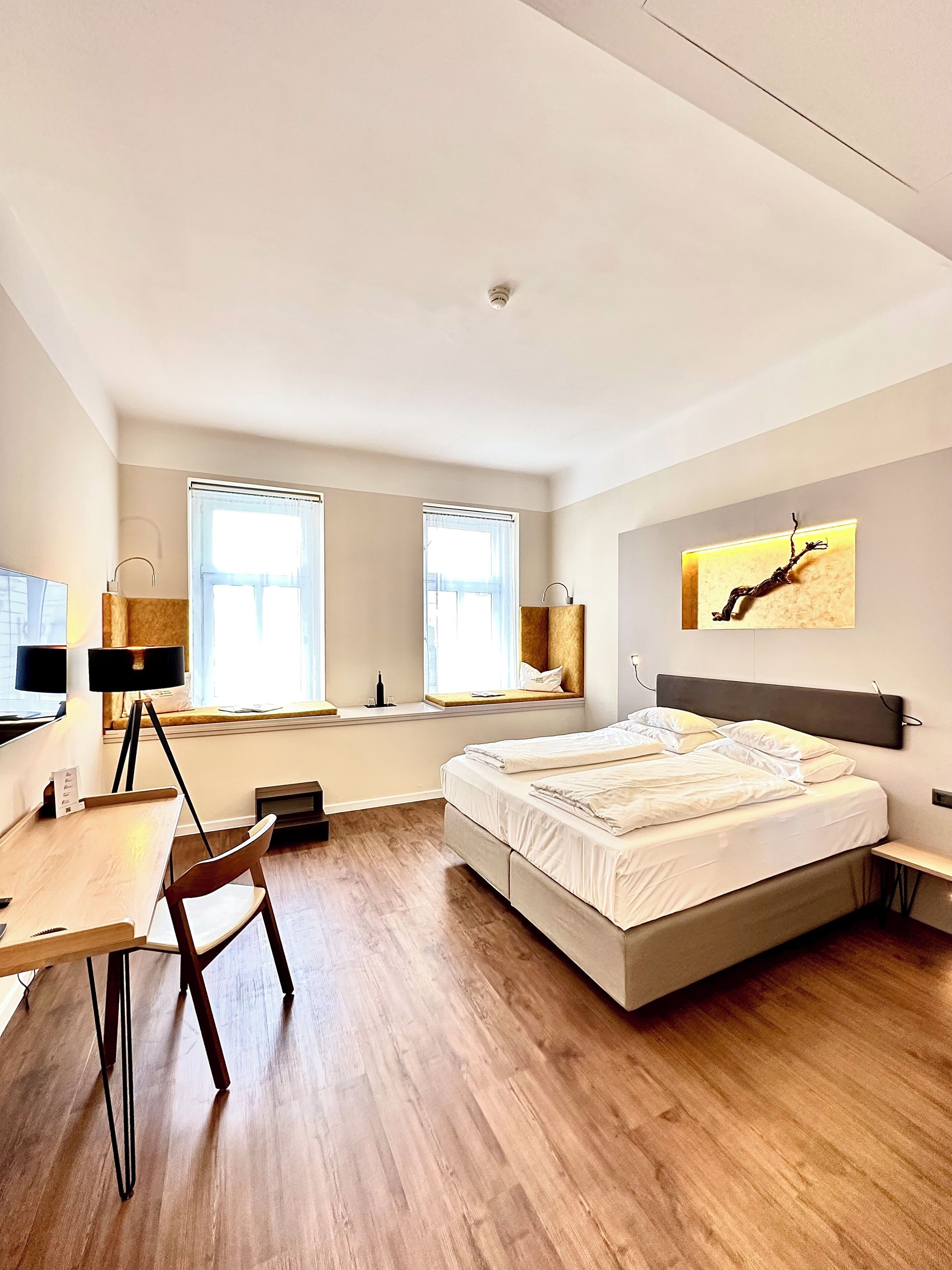Quarto moderno com uma cama grande, uma escrivaninha e duas janelas.