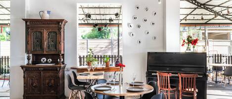 Uma sala de jantar com piano, cadeiras, uma mesa posta para dois e um aparador decorativo.