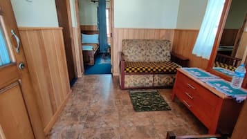 Quarto compacto com cama, sofá, armário de madeira e uma pequena mesa com espelho.