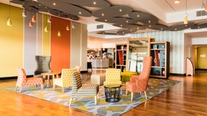 Um lobby moderno com área de estar central, cozinha ao fundo e um espelho grande refletindo o espaço.