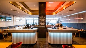 Um restaurante moderno com um bar central, cabines e um teto alto com iluminação embutida.