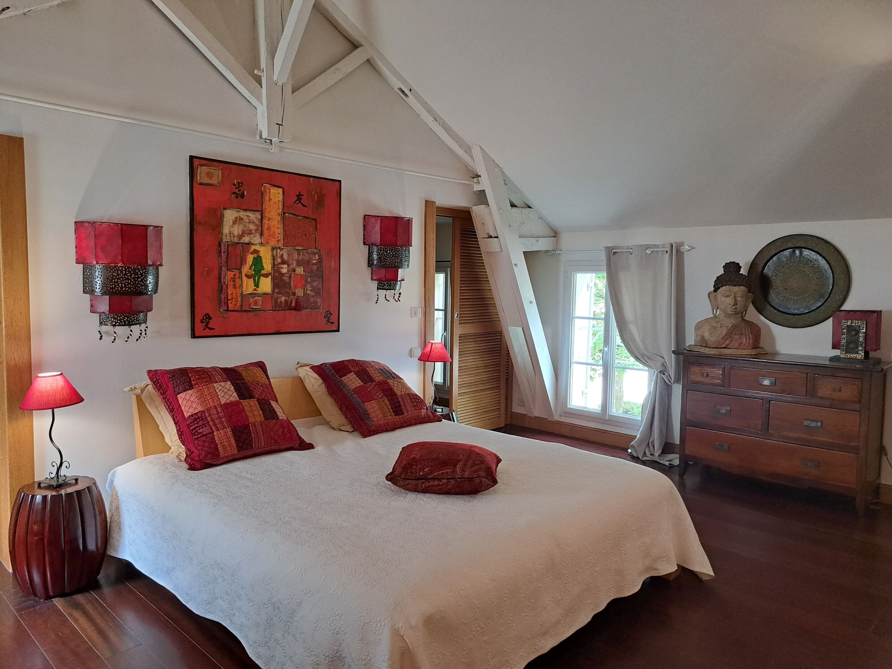 Quarto com cama grande, cómoda de madeira, estátua de Buda e obra de arte vermelha na parede.