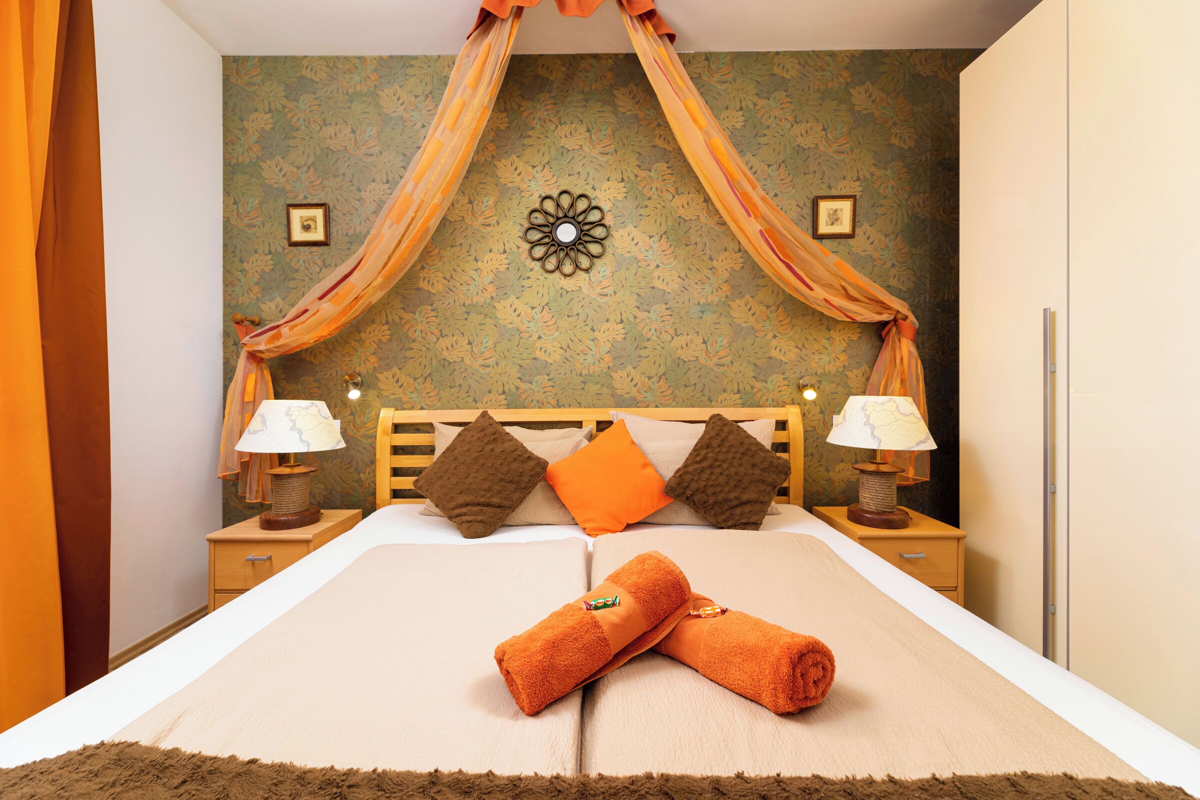Uma cama bem arrumada com duas almofadas, um objeto decorativo na parede e duas luminárias de cabeceira.