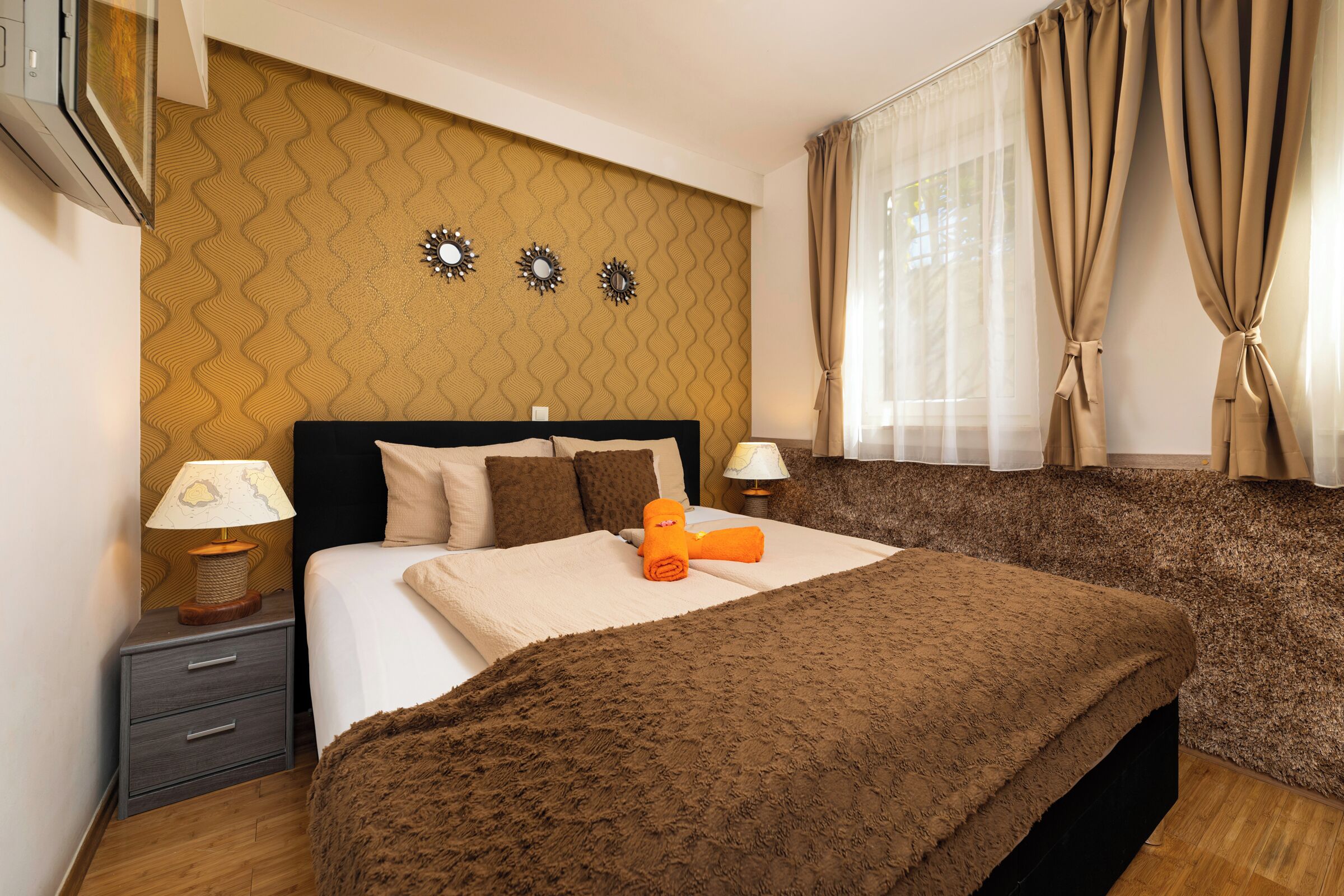 Quarto de hotel com cama, mesas de cabeceira, janela com cortinas e decoração de parede.