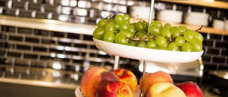 Uma banca de frutas em três níveis, com uvas verdes no nível superior, pêssegos no nível do meio, e um prato branco com pêssegos no nível inferior.