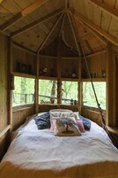 Quarto de cabana de madeira com cama, almofadas e janela com vista para uma floresta.