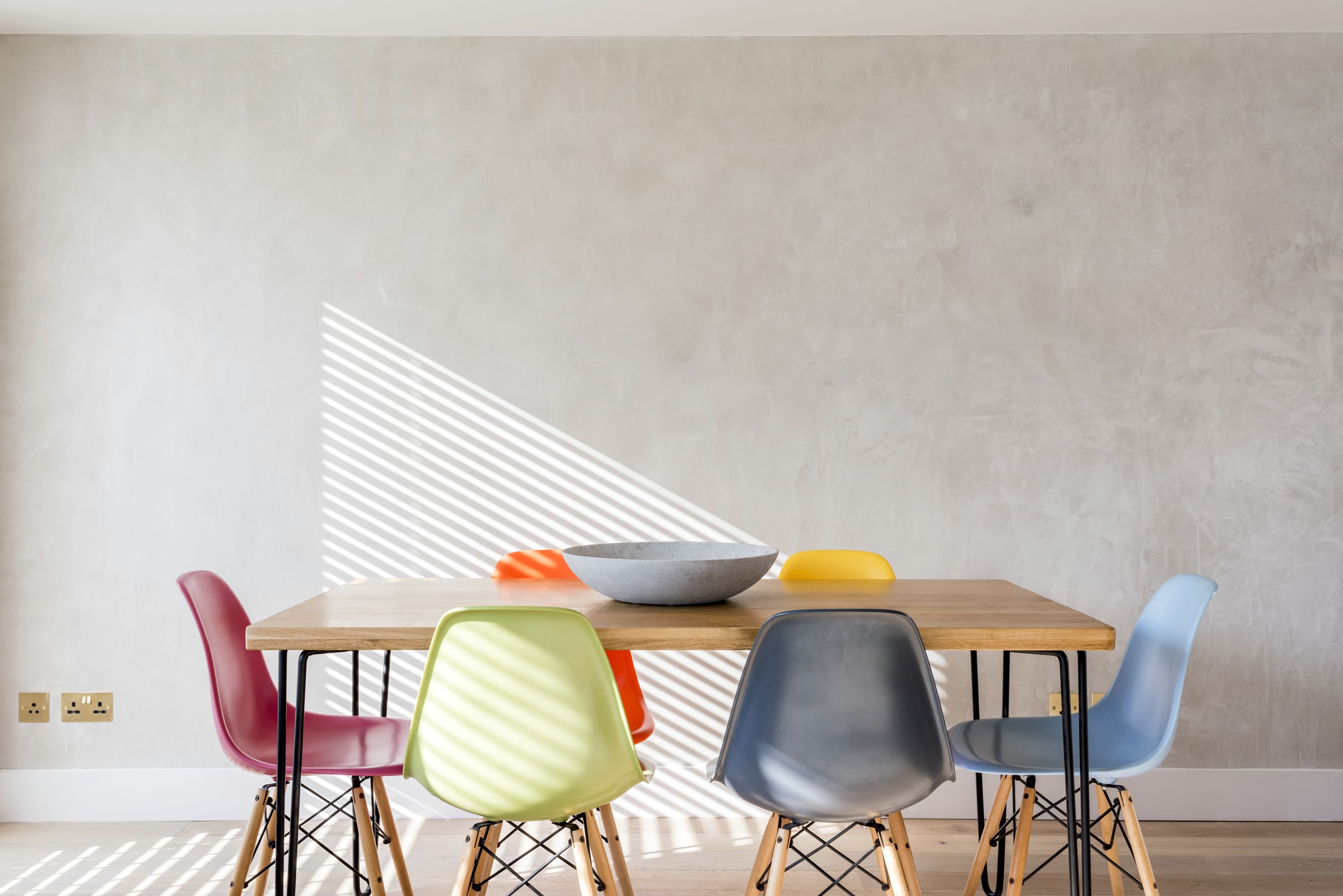 Uma área de refeições com mesa de madeira e cadeiras coloridas.