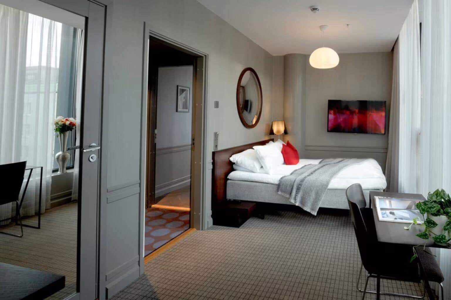 Quarto de hotel moderno com cama, mesa de cabeceira, cadeira e escrivaninha com cadeira.