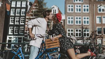 Um casal se beijando em uma bicicleta em frente a uma fileira de edifícios europeus tradicionais.