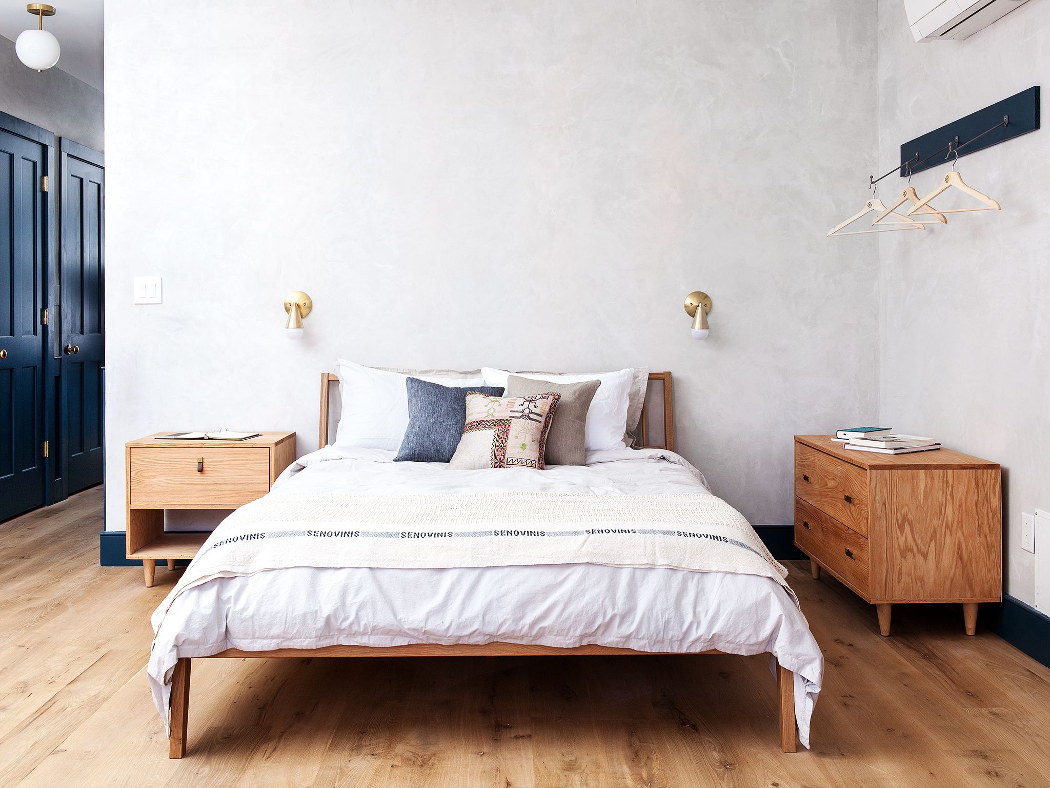 Quarto com cama de madeira, mesas de cabeceira, guarda-roupa e um varal fixado na parede.